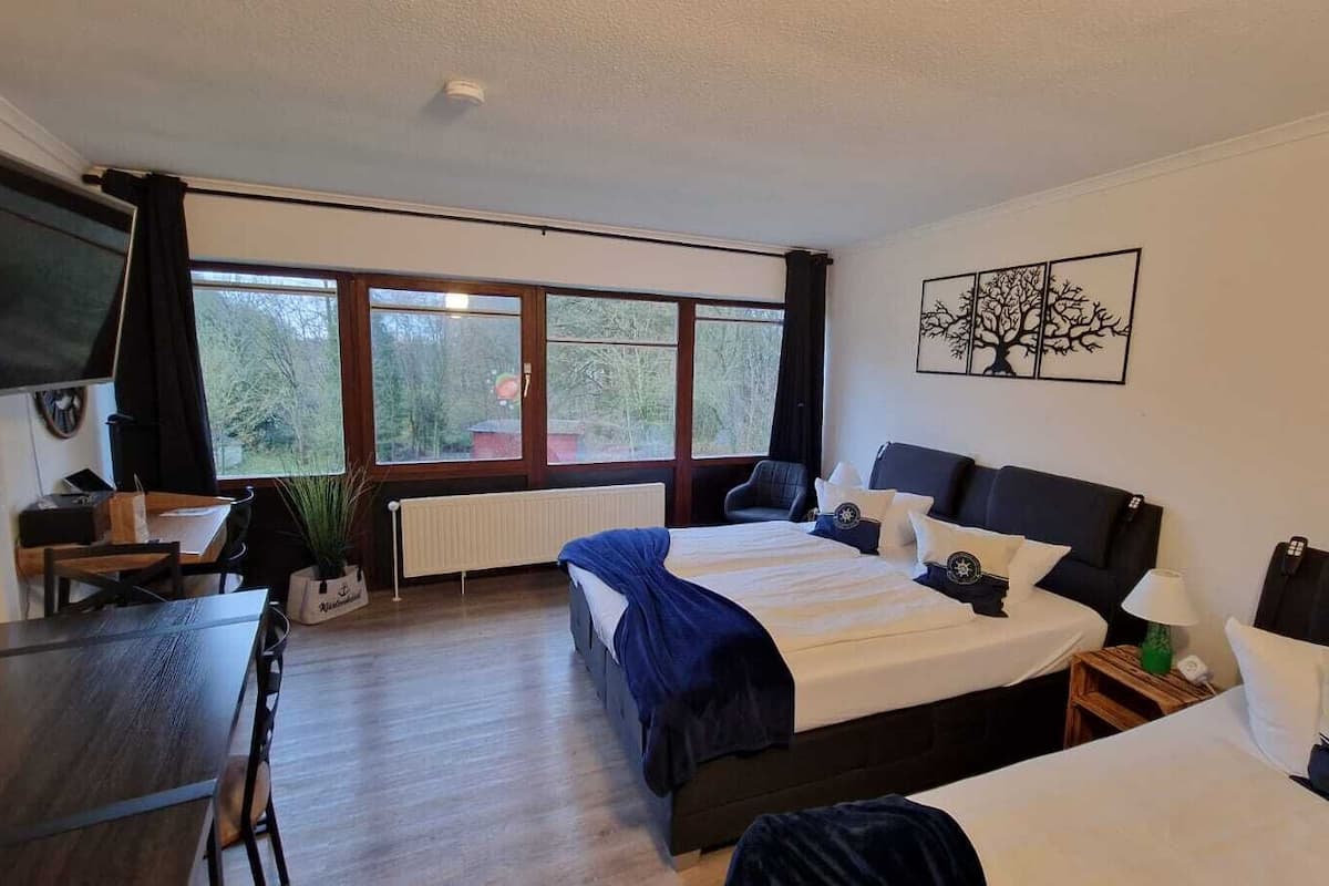 Quarto de hotel com cama grande, uma escrivaninha e janela com vista para árvores.