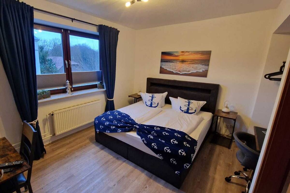 Quarto com cama, janela com cortinas, quadro na parede e radiador.