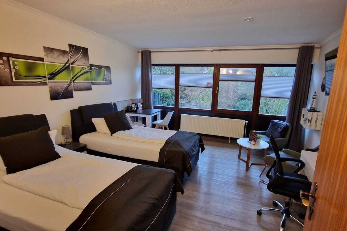 Quarto de hotel com duas camas, uma secretária pequena, uma cadeira e vista para o exterior.