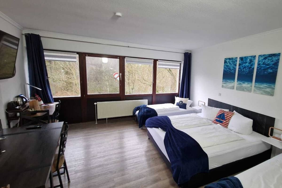 Quarto de hotel com duas camas, uma escrivaninha e janela com vista para árvores.