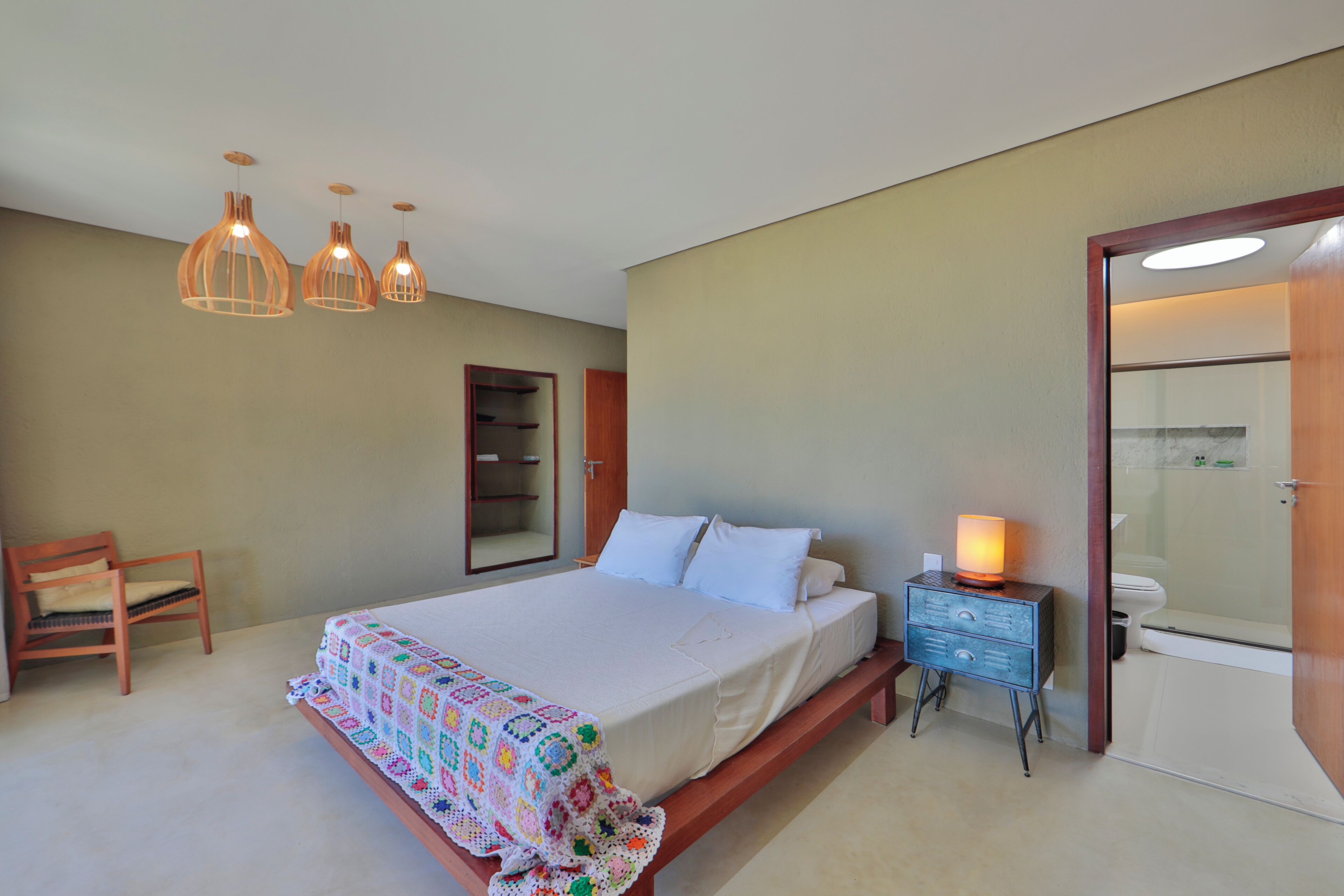 Quarto com cama, mesa de cabeceira, luminária, cadeira e espelho.