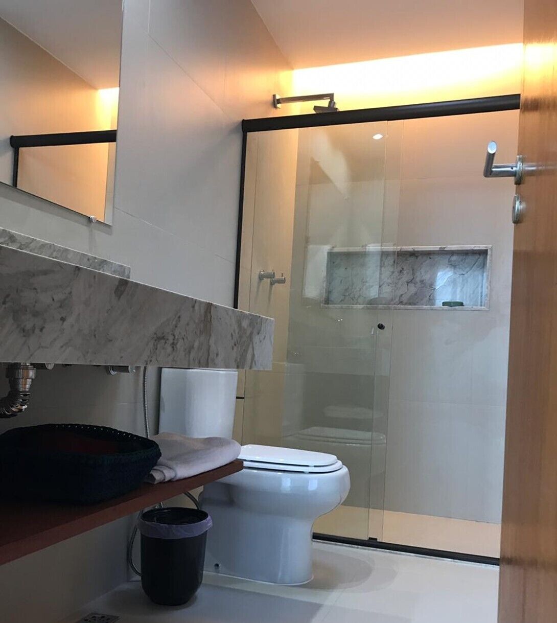 Uma casa de banho moderna com cabine de duche em vidro, lavatório com bancada de mármore e sanita.