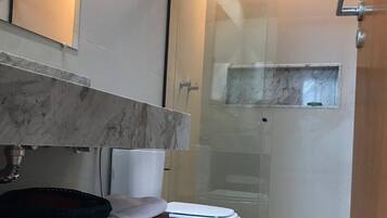 Uma casa de banho moderna com cabine de duche em vidro, lavatório com bancada de mármore e sanita.