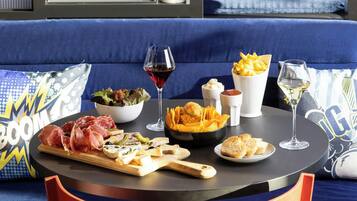 Mesa redonda com diversos alimentos e bebidas, colocada sobre um sofá azul com almofadas combinando.