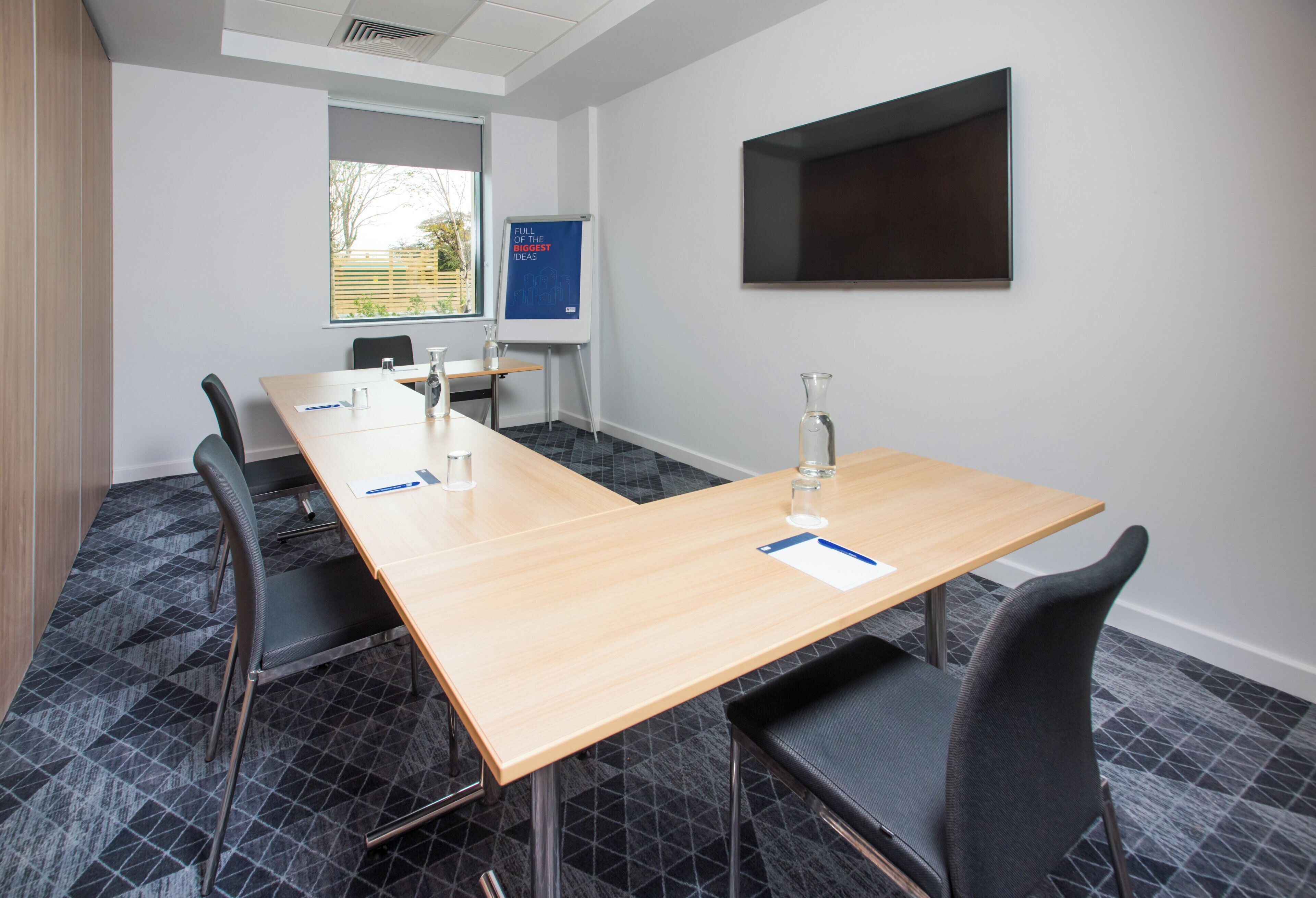 Uma sala de conferência com uma mesa comprida, cadeiras, tela de projetor e um quadro branco.