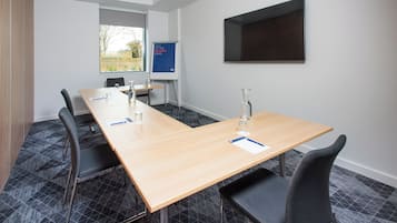 Uma sala de conferência com uma mesa comprida, cadeiras, tela de projetor e um quadro branco.