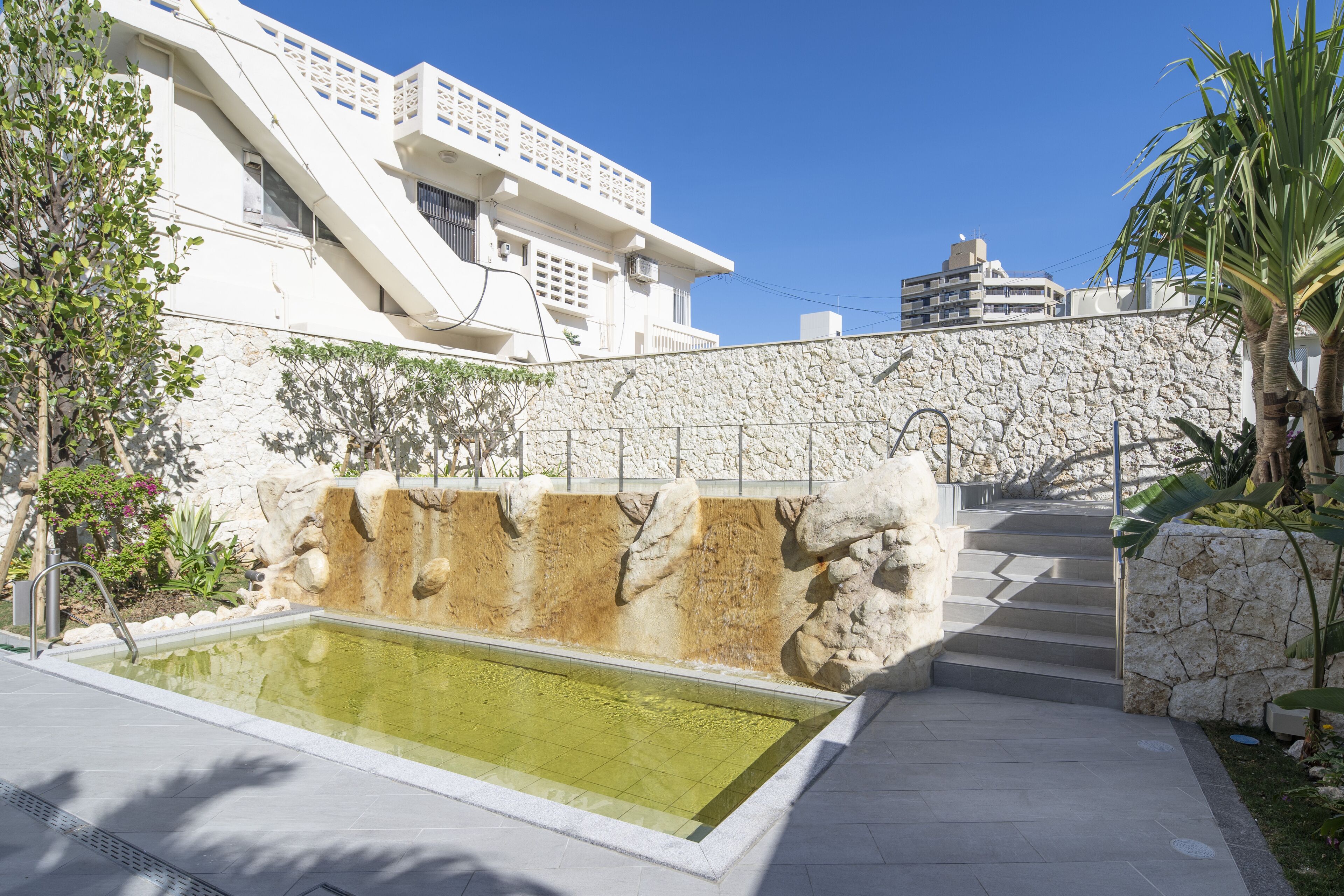 Piscina com muro de pedra e degraus que levam a um edifício.