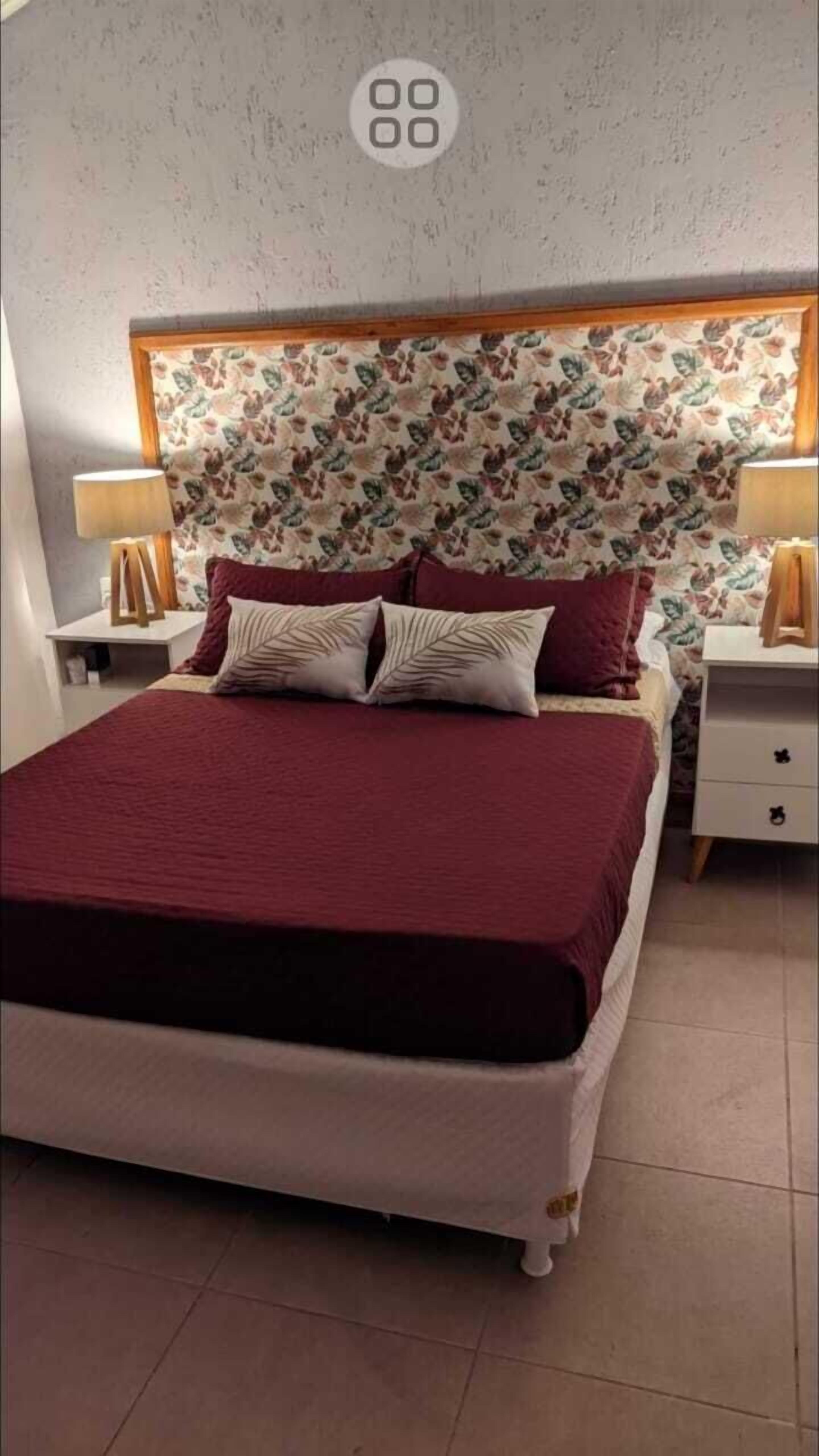 Quarto com uma cama grande, papel de parede floral, duas mesas de cabeceira com abajures e uma pequena mesinha de apoio.