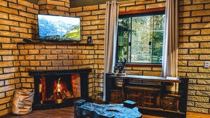 Quarto acolhedor com parede de tijolos, lareira, televisão e janela com vista para o verde.