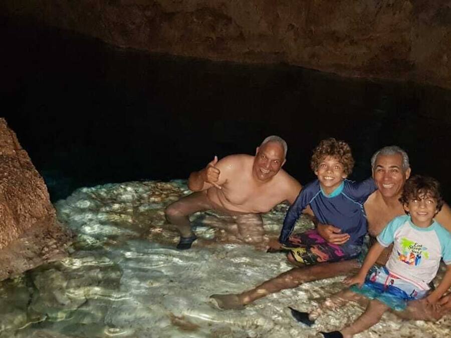 Um grupo de pessoas sentadas em um ambiente semelhante a uma caverna, com água cristalina.