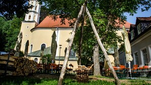 Igreja com campanário, mesas ao ar livre e árvores.