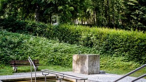 Piscina de concreto com grades de metal, rodeada por um calçadão pavimentado e um banco.