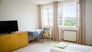 Quarto de hotel com duas camas, televisão, escrivaninha, cadeira e janela com vista para o campo.