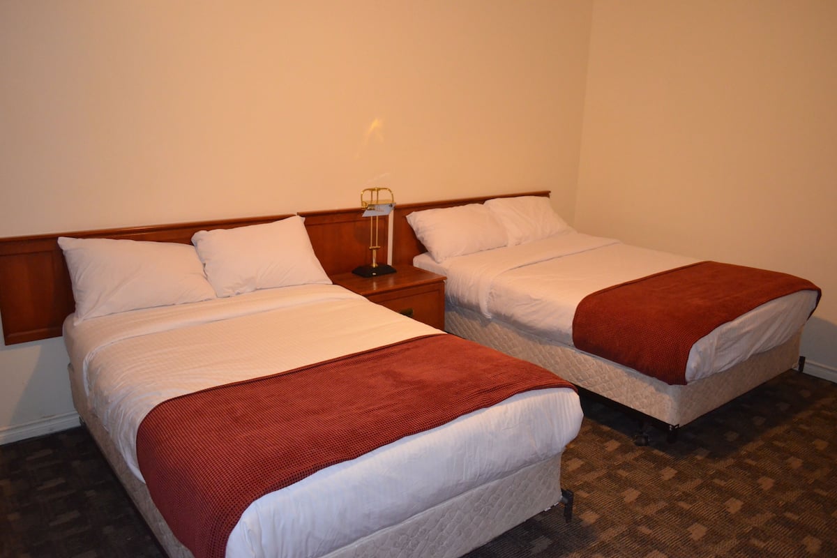 Duas camas de solteiro com cabeceiras de madeira, roupa de cama branca e um cobertor vermelho em cada uma.