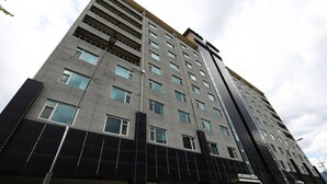 Um edifício de vários andares com design arquitetônico moderno, apresentando uma série de janelas retangulares e um telhado plano.