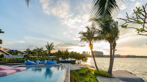 Uma piscina com cadeiras de descanso azuis, uma palmeira e vista para o pôr do sol.