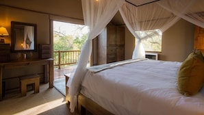 Quarto com cama, mesa de cabeceira e janela com vista para árvores.