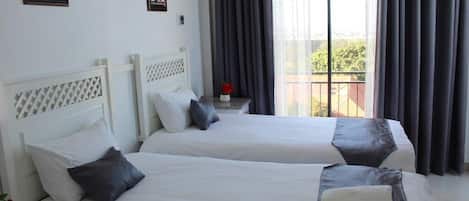 Quarto de hotel com duas camas, cabeceiras brancas e vista para a varanda.