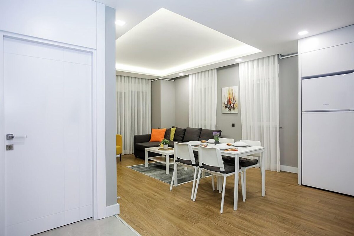 Uma sala de estar moderna com área de jantar, paredes brancas e iluminação no teto.