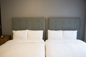 Cama de casal com cabeceira estofada cinza e roupa de cama branca.