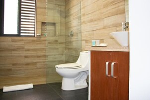 Um banheiro moderno com box de vidro, vaso sanitário branco e toucador de madeira com pia.