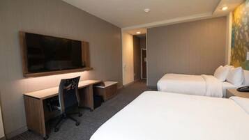 Quarto de hotel com uma grande televisão de tela plana na parede, uma escrivaninha com cadeira e duas camas de solteiro.