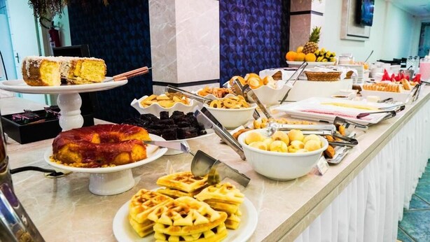 Buffet com diversos alimentos, incluindo waffles, bolos e frutas.