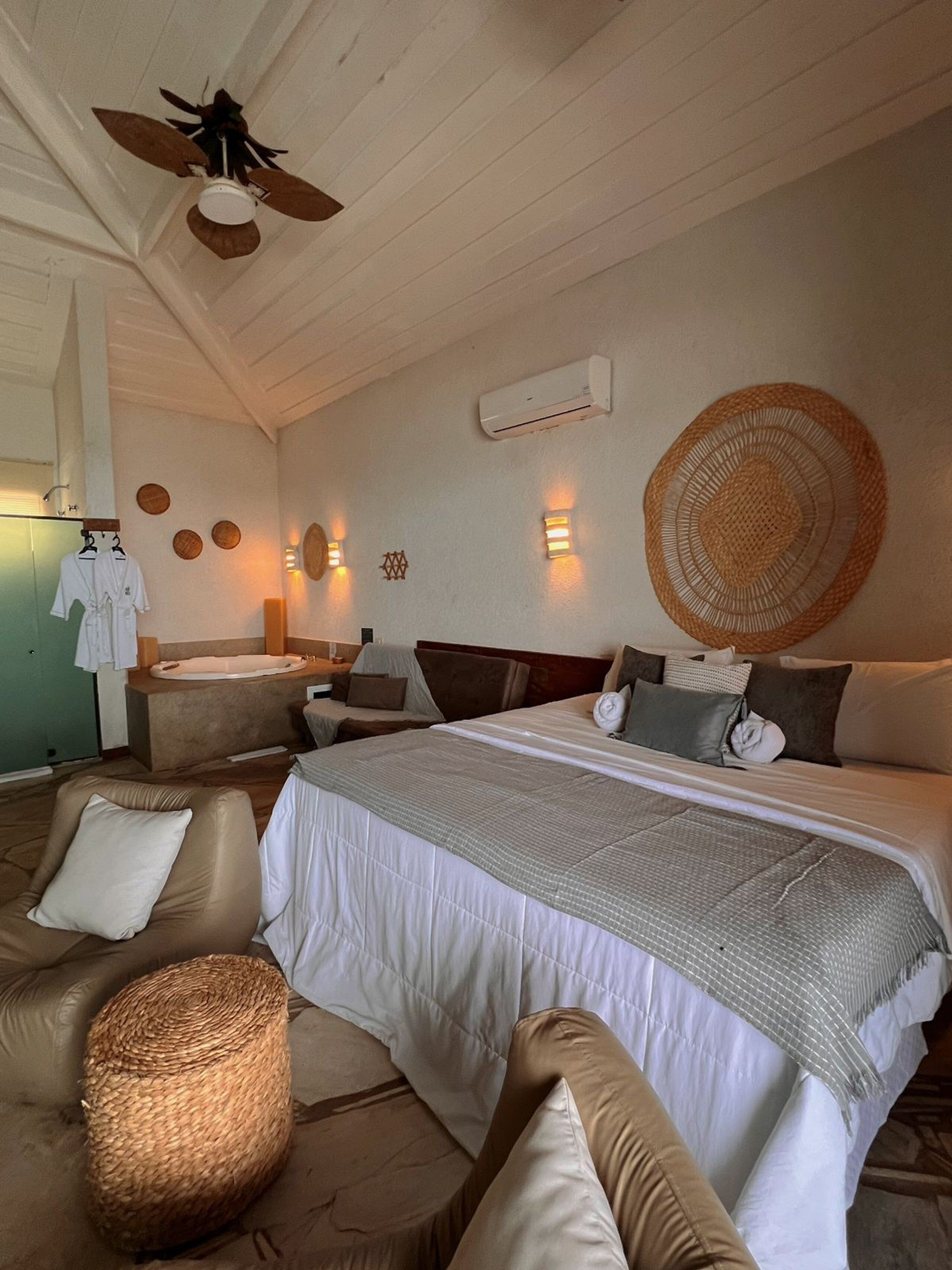 Quarto espaçoso com cama grande, ventilador de teto, banheiro com banheira e ar-condicionado de parede.