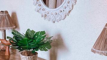Um console de madeira com uma cesta trançada contendo uma planta verde, um espelho de macramé e uma corda franzida.