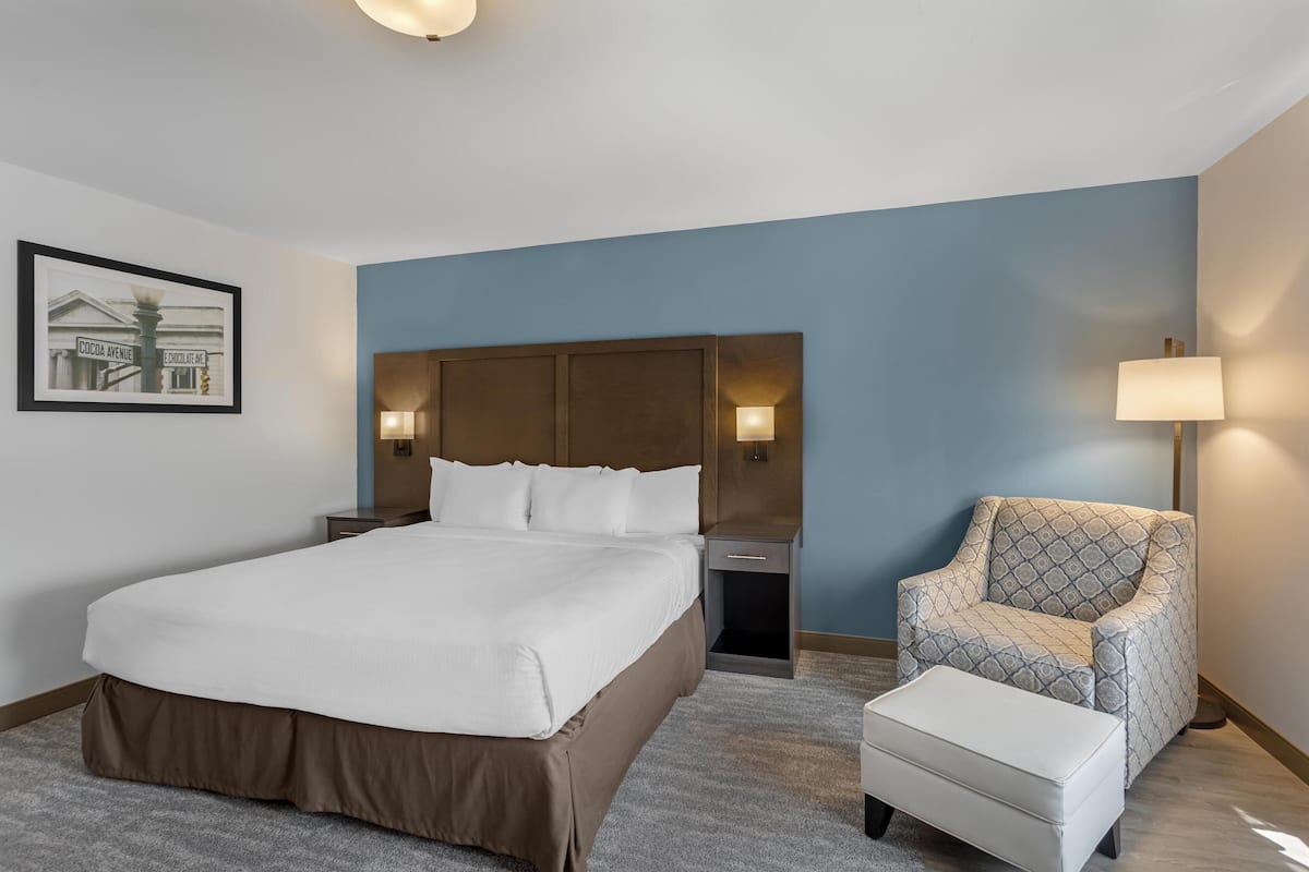 Quarto de hotel com uma cama grande, uma mesa de cabeceira, uma cadeira e uma pequena mesa.