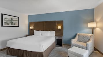 Quarto de hotel com uma cama grande, uma mesa de cabeceira, uma cadeira e uma pequena mesa.