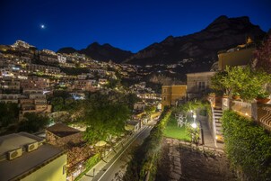 Vista noturna de uma vila em encosta, com edifícios, uma escadaria e um pequeno jardim.