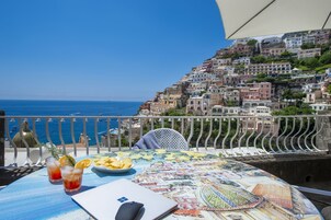 Terraço com mesa posta para dois, com vista para uma cidade costeira e edifícios coloridos.