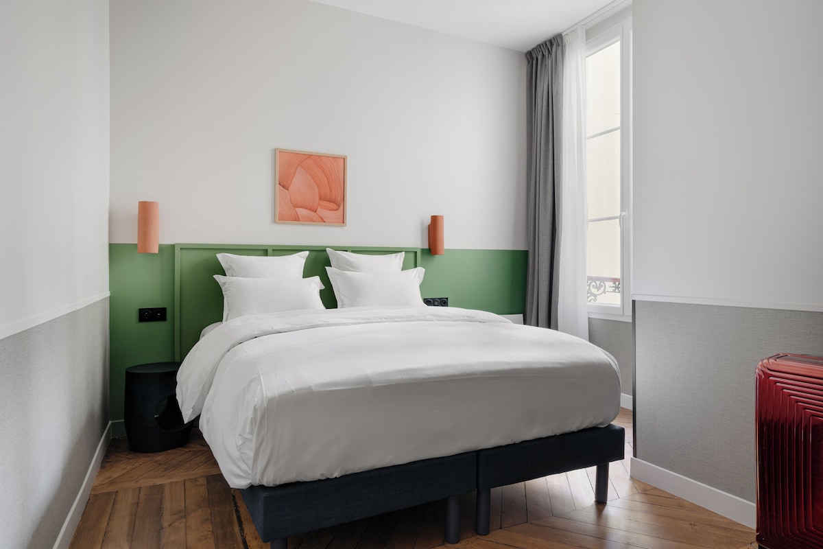 Quarto moderno com cabeceira verde, roupa de cama branca e uma única obra de arte sobre a cama.
