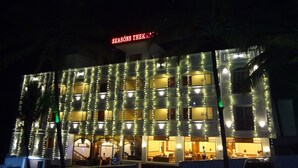 Um hotel com vários andares, iluminado por luzes de cordão, e uma placa com a inscrição "SEASONS THEK".