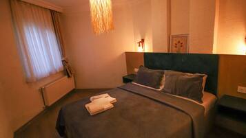 Quarto de hotel com uma cama grande, luminária pendente e janela com cortinas.