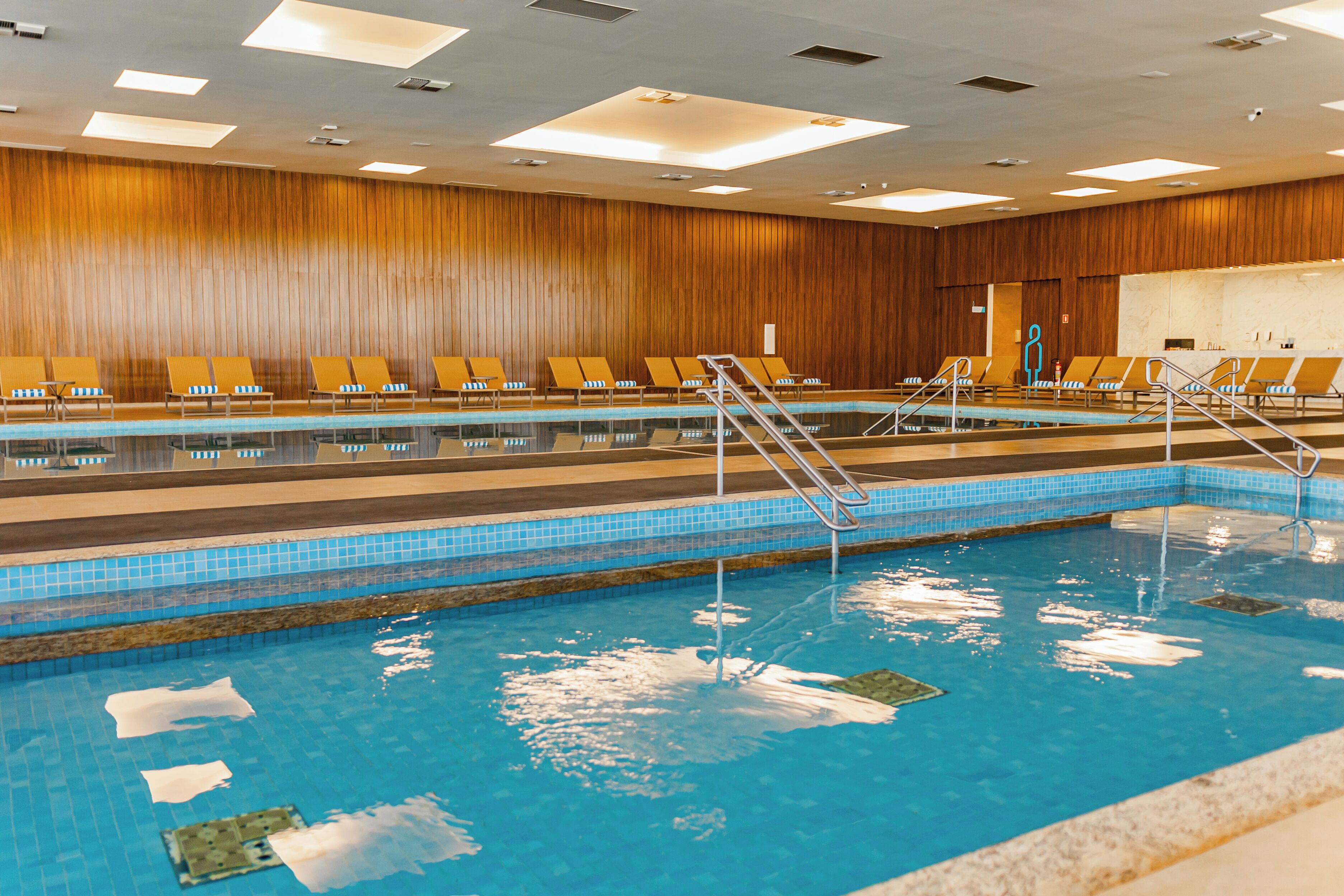 Piscina interna com várias pistas de natação, paredes de painel de madeira e espreguiçadeiras.
