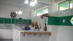 Uma área de recepção com balcão branco, decorações na parede em tons de verde e um relógio pendurado.