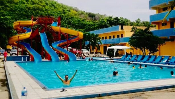 Uma piscina com escorregador aquático, cercada por um edifício com várias varandas.