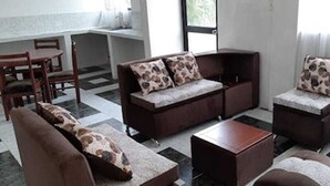 Uma sala de estar com sofá marrom, uma mesa de centro e um espaço de jantar com mesa e cadeiras.