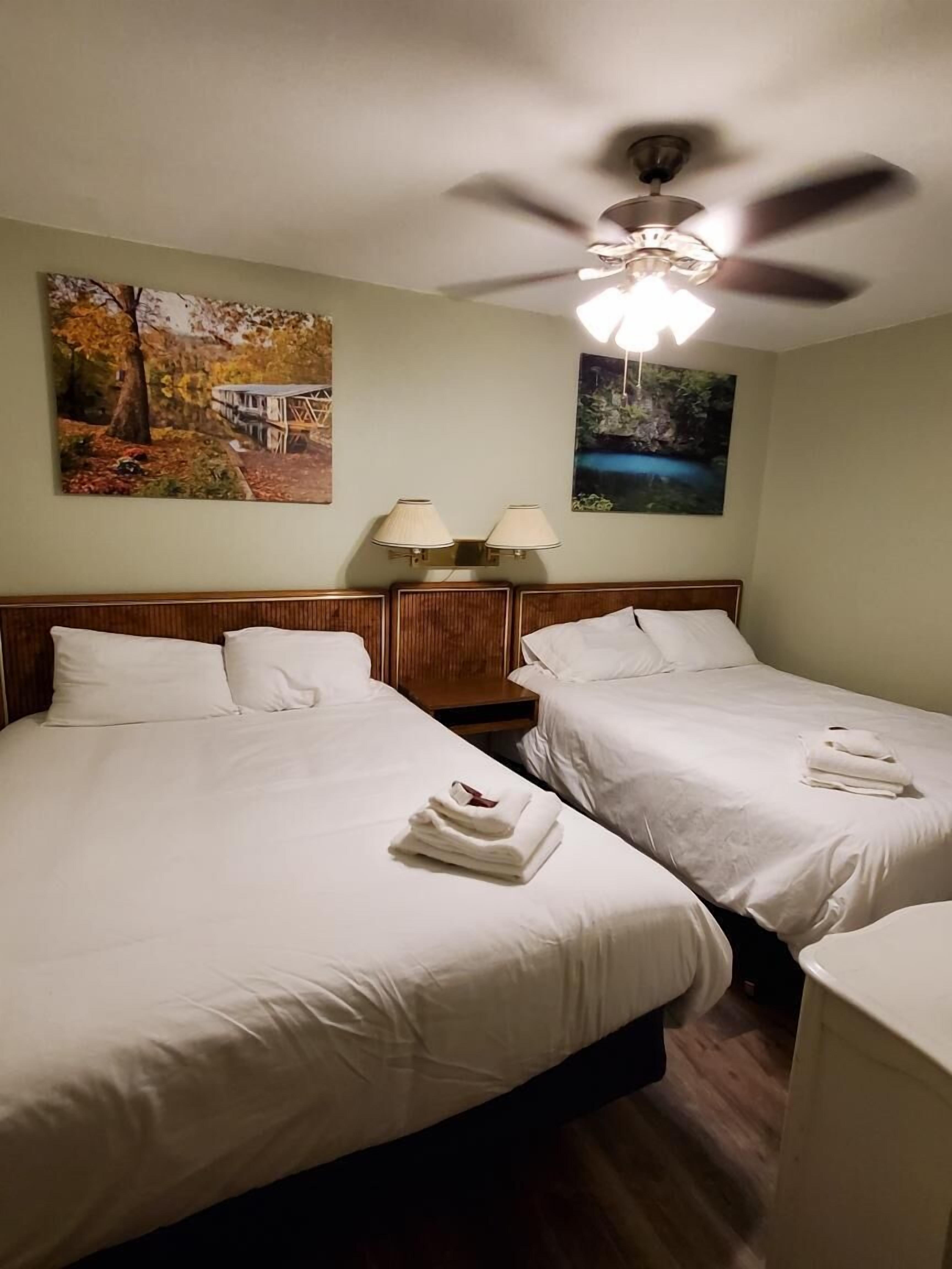 Quarto de hotel com duas camas, ventilador de teto e obras de arte nas paredes.