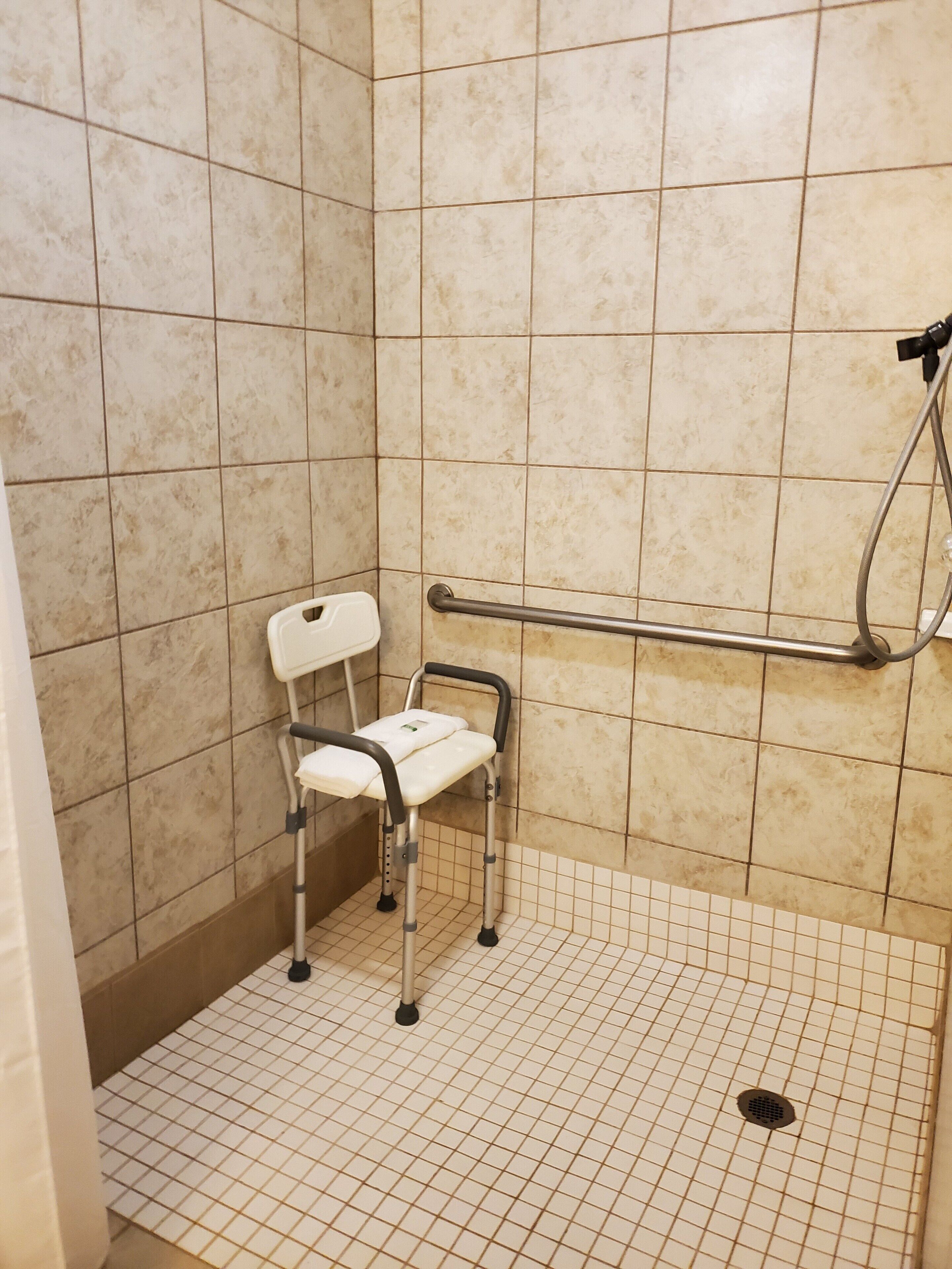 Um banheiro com piso de azulejos brancos, vaso sanitário branco e barra de apoio na parede.