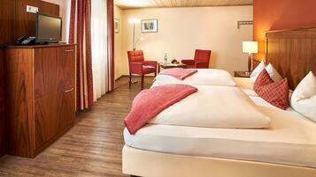 Quarto de hotel com duas camas, uma mesa, uma cadeira, uma TV e um abajur.