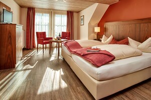 Quarto de hotel com uma cama grande, uma escrivaninha com cadeira, televisão e uma janela com cortinas.