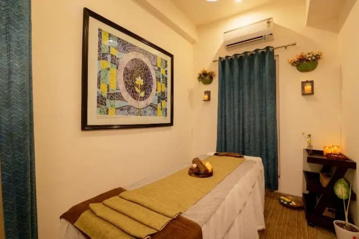 Quarto com cama, uma obra de arte emoldurada na parede, aparelho de ar condicionado, mesa pequena com velas e um vaso de planta.