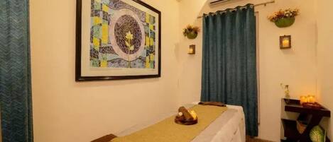 Quarto com cama, uma obra de arte emoldurada na parede, aparelho de ar condicionado, mesa pequena com velas e um vaso de planta.