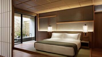 Quarto de hotel moderno com uma cama grande, painéis de madeira e uma porta de vidro deslizante para uma área externa.
