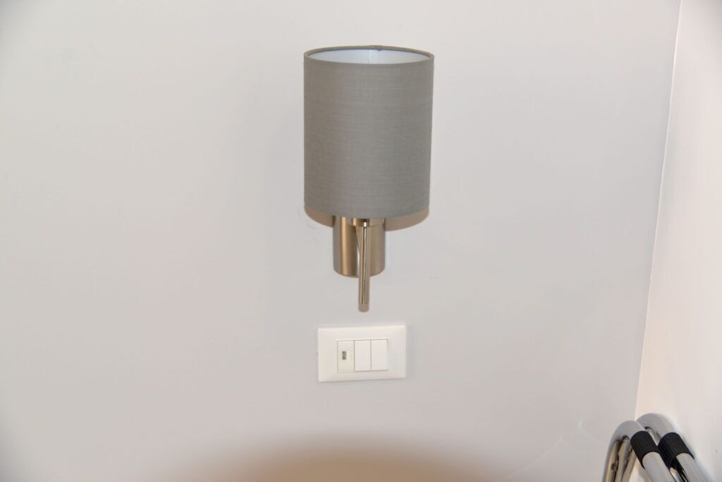 Luminária de parede com cúpula cilíndrica e interruptor abaixo.