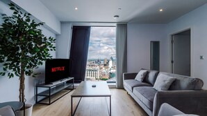 Uma sala de estar moderna com uma janela grande, uma TV de tela plana, um sofá cinza e um vaso de planta.