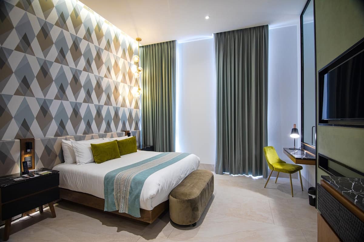 Quarto de hotel moderno com uma cama grande, uma mesa, uma cadeira e uma televisão.